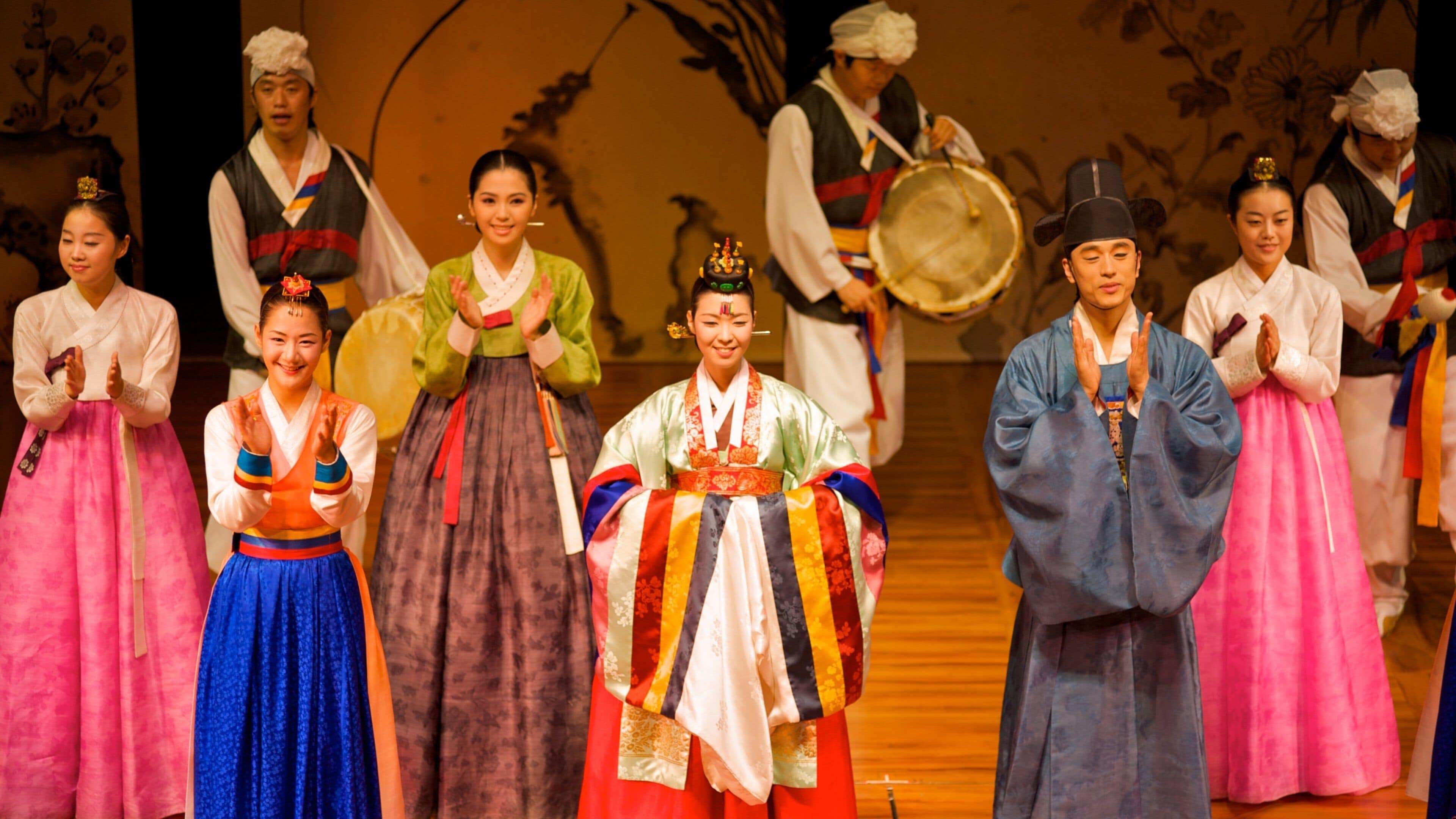 Um grupo de pessoas vestidas com hanbok tradicionais coreanos se apresentando em um palco.