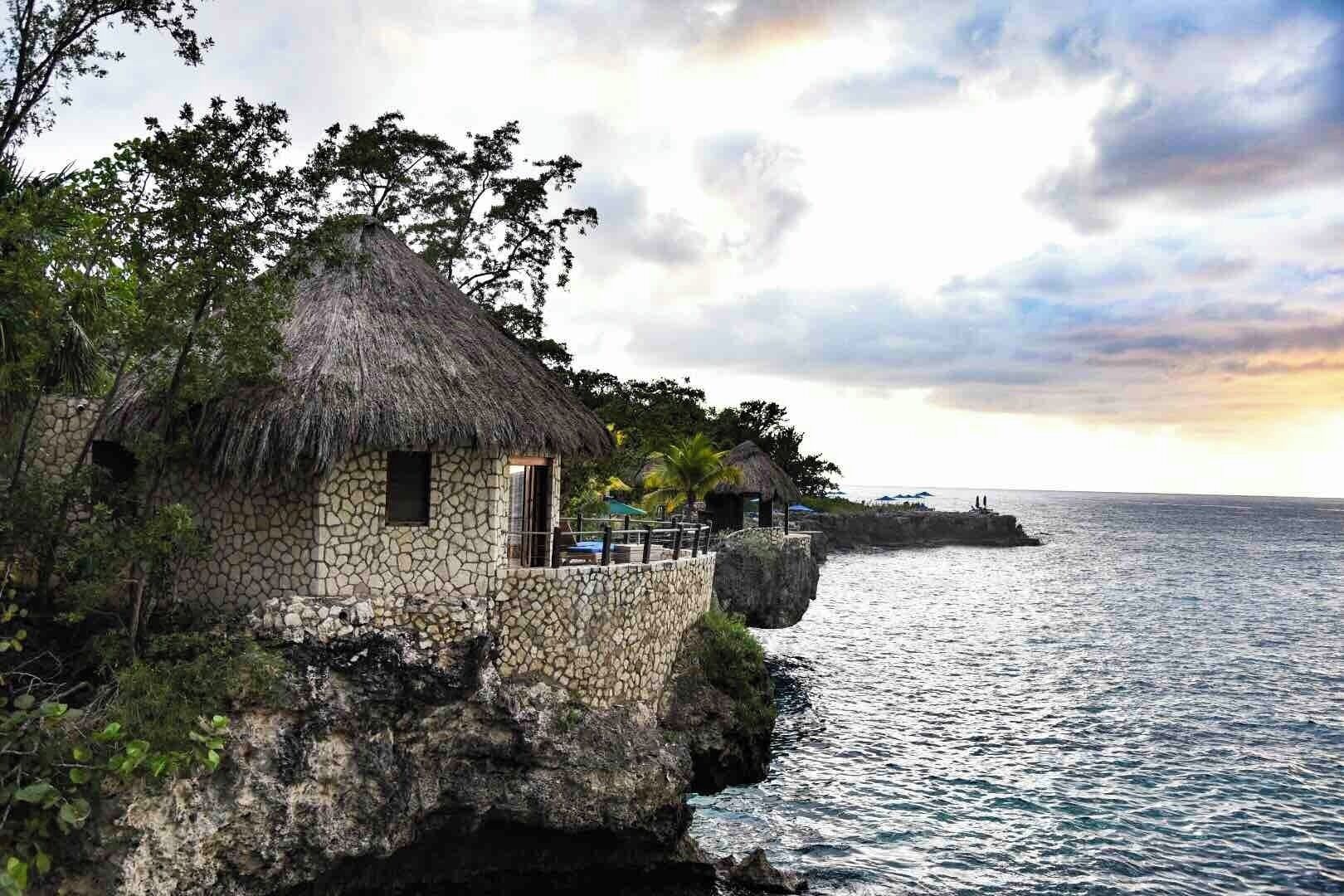 Uma casa com telhado de palha e parede de pedra, com vista para um corpo de água.