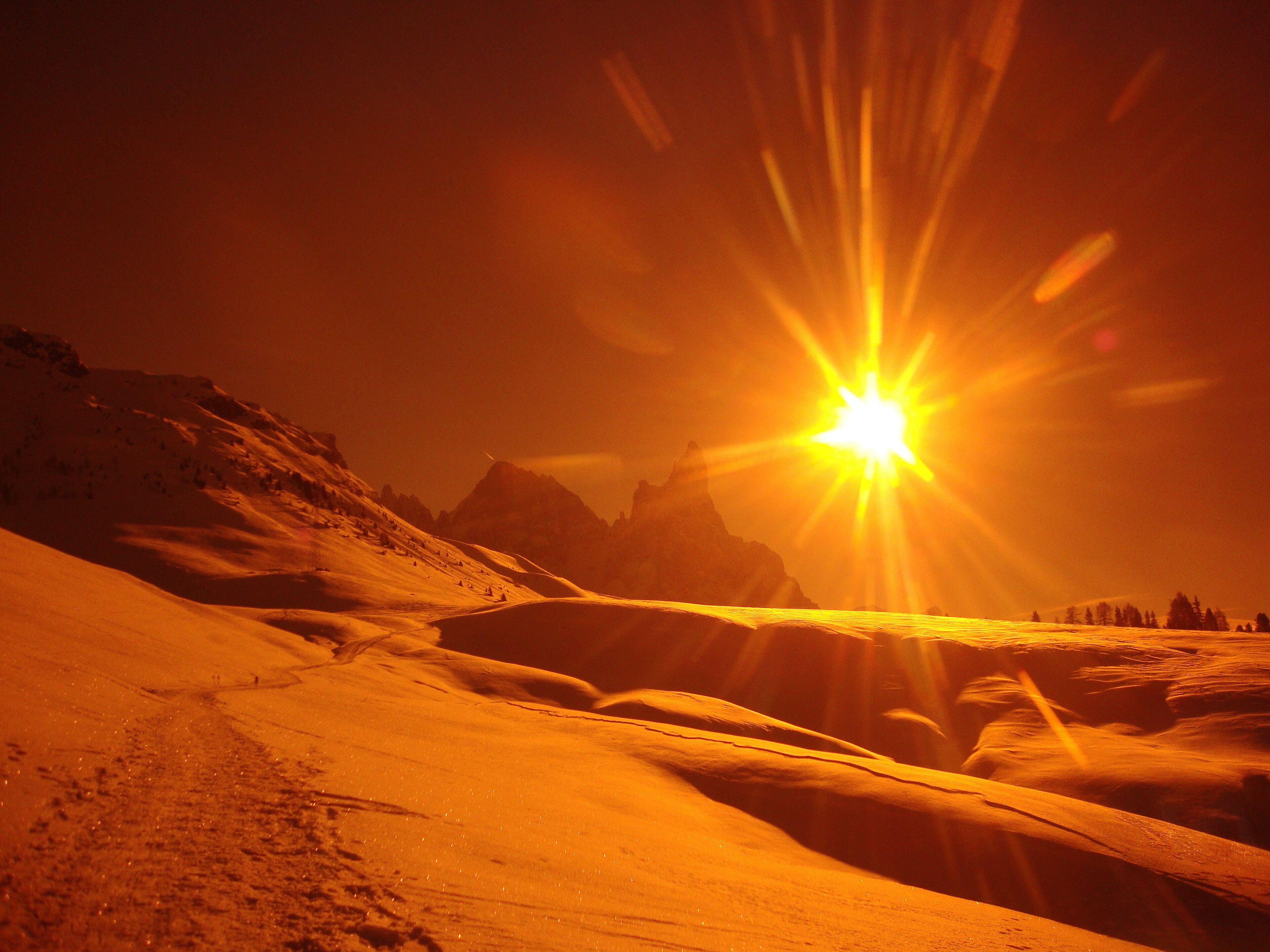 Paisagem montanhosa coberta de neve, com um sol brilhante a brilhar.