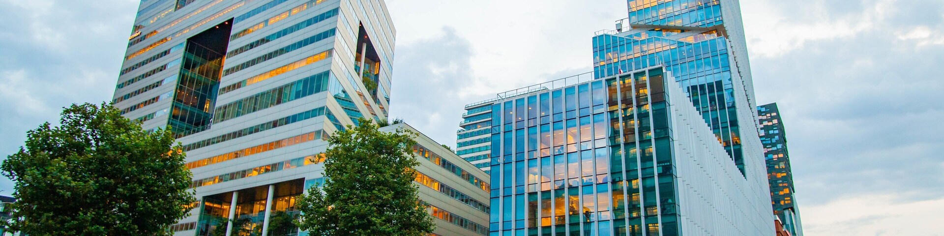 Uma praça urbana moderna com edifícios de vidro contemporâneos, árvores e áreas de estar ao ar livre.