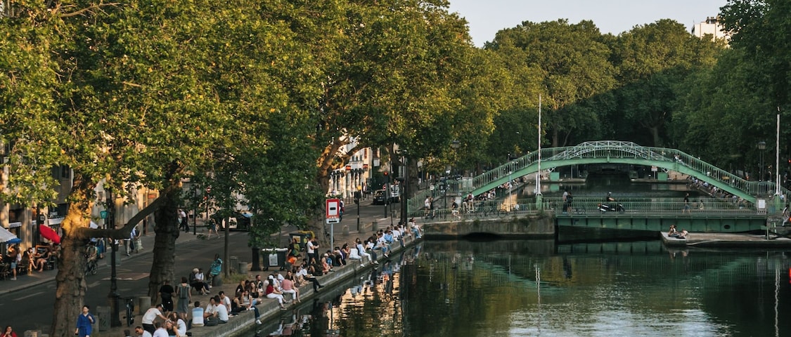 Um rio calmo com uma ponte, árvores e um edifício ao fundo.