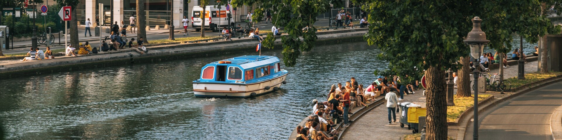Um rio com um barco, pessoas sentadas na margem e árvores ao longo da área.