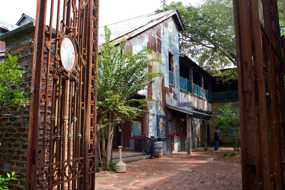 Um edifício rústico com um portão de metal, paredes de tijolo e uma árvore em primeiro plano.