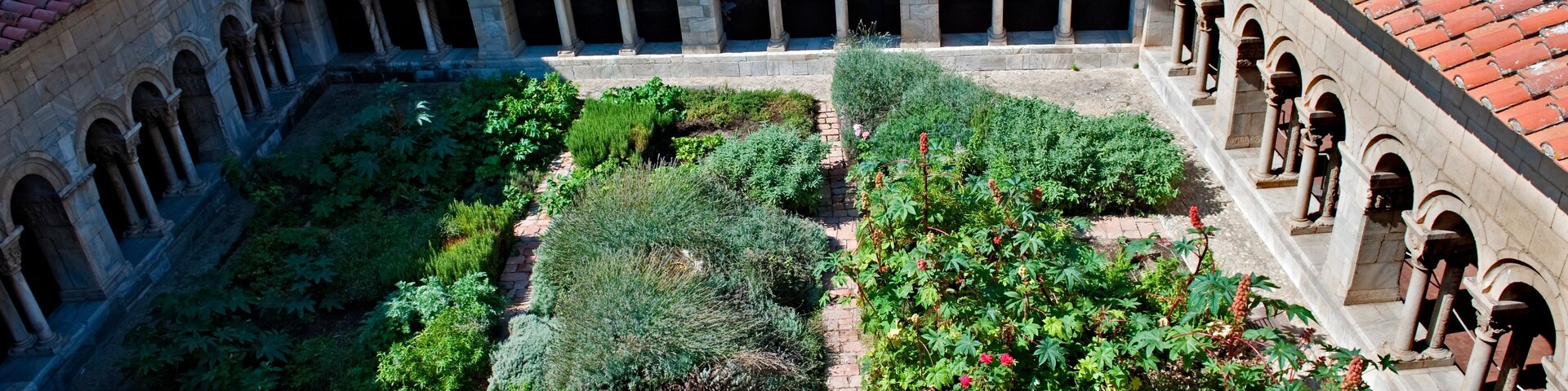 Um pátio com telhados de telha vermelha, arcos de pedra e plantas verdes.