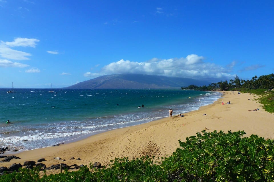 Uma praia com águas azuis cristalinas, areal arenoso e montanha ao fundo.