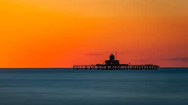 Um cais se estendendo sobre águas calmas ao pôr do sol.