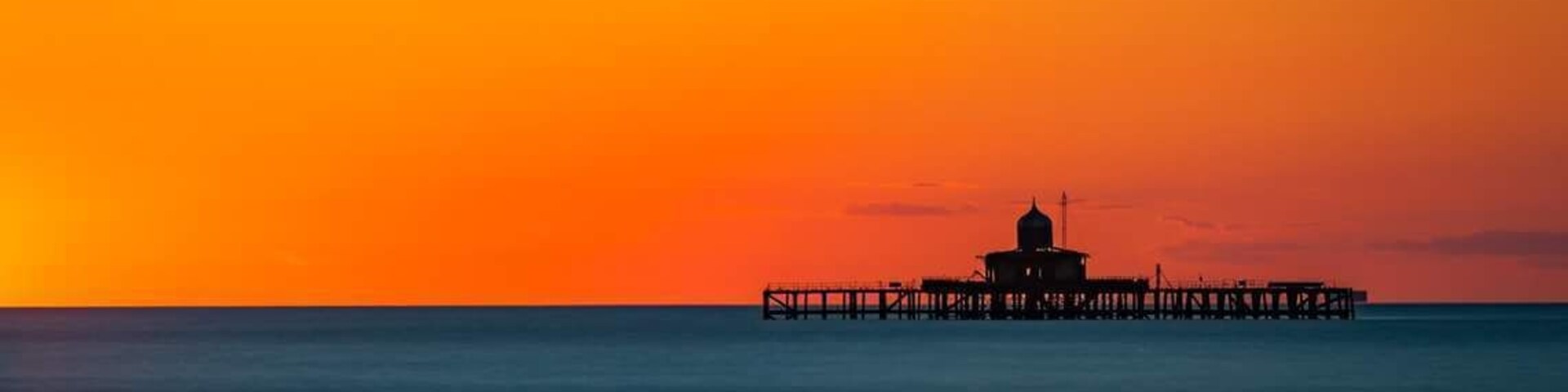 Um cais se estendendo sobre águas calmas ao pôr do sol.