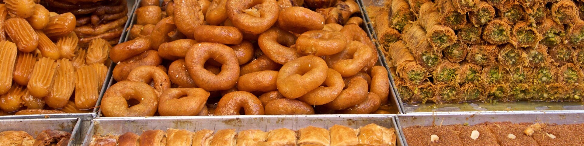 Diversos produtos de panificação, como doces, donuts e biscoitos, dispostos em bandejas.