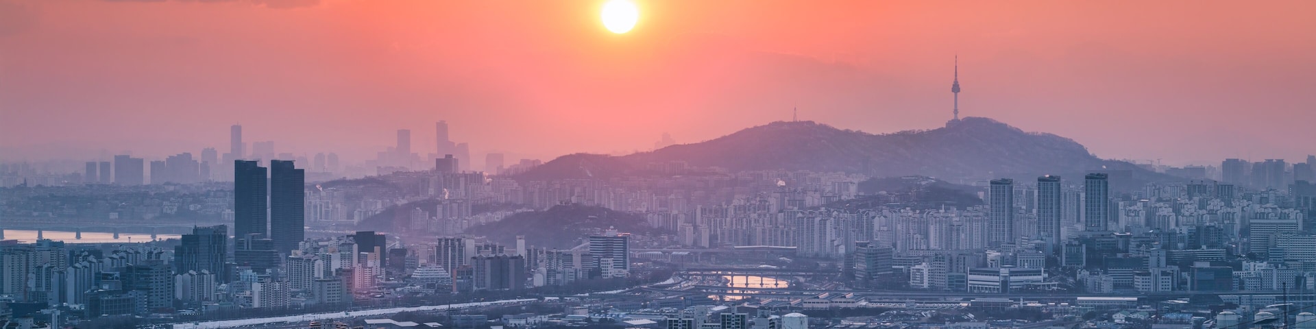 Vista urbana ao pôr do sol, com uma torre imponente e um rio.