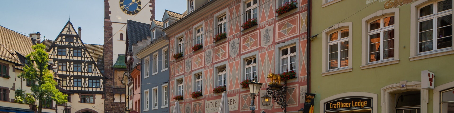 Uma cidade histórica europeia com uma torre do relógio imponente, edifícios coloridos e um pub de cerveja artesanal.