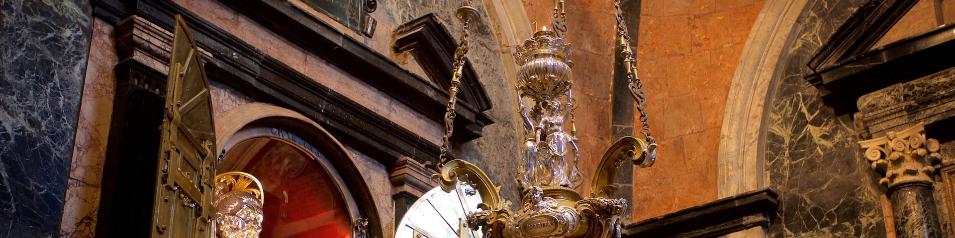 Um lustre ornamentado, paredes de mármore e uma estátua em um interior imponente.