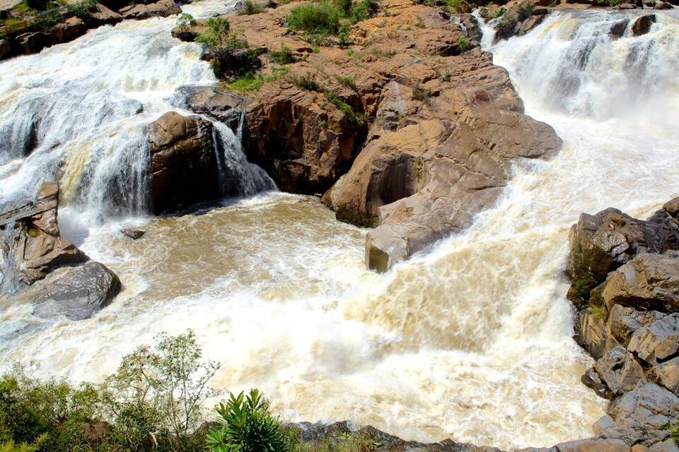 Uma cachoeira imponente despencando sobre terreno rochoso, com vegetação exuberante ao redor.