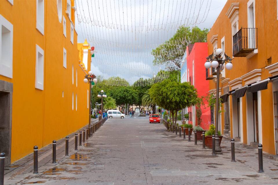 Uma rua estreita ladeada por edifícios coloridos, um carro vermelho estacionado na lateral e um pavimento molhado.