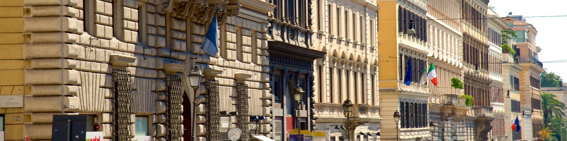 Uma rua flanqueada por edifícios históricos, bandeiras e pedestres.