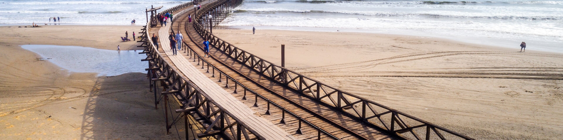 Um calçadão de madeira que se estende até o oceano, com pessoas caminhando.