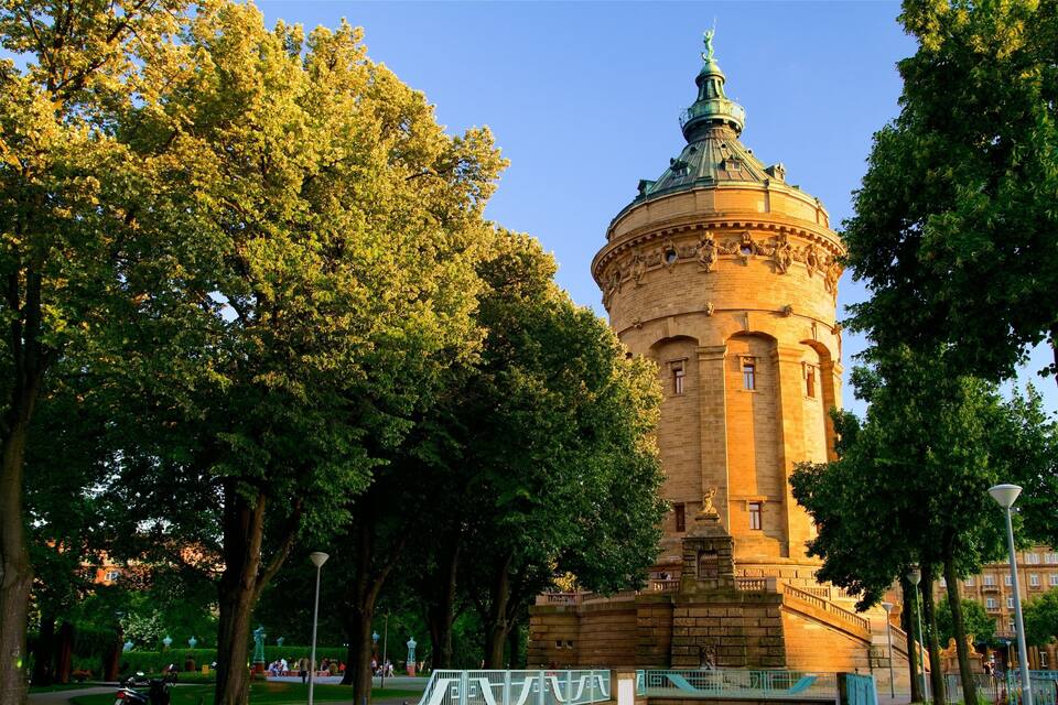 Uma torre histórica com cúpula e estátua, cercada por árvores verdes e exuberantes.
