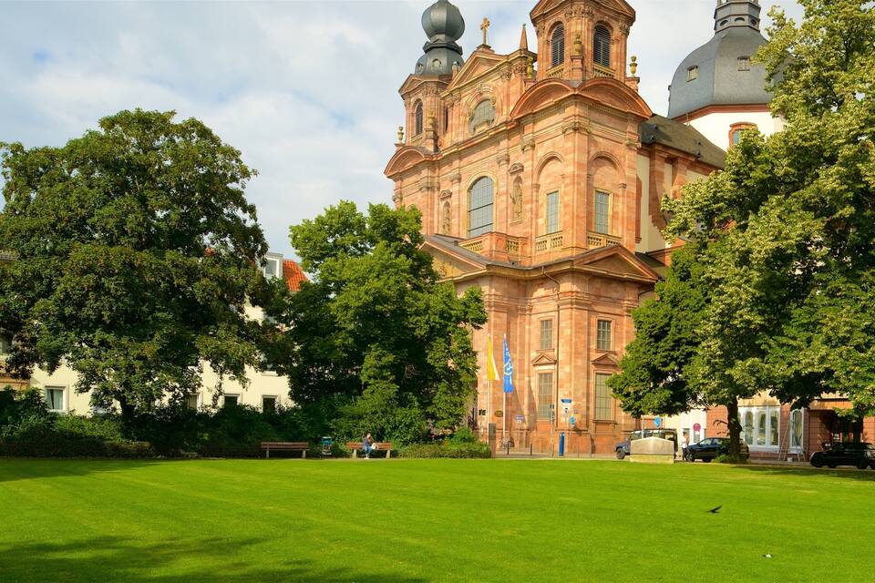 Um edifício histórico com arquitetura ornamentada, rodeado por árvores verdes exuberantes e um jardim bem cuidado.