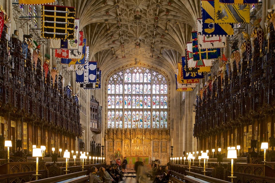 Interior de uma catedral com decorações requintadas, janelas de vitrais e um teto abobadado alto.