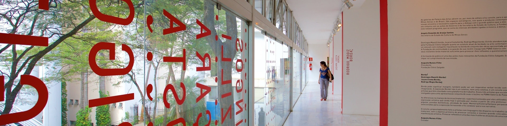 Um corredor com letras vermelhas grandes na parede de vidro, uma pessoa caminhando e uma escada à esquerda.