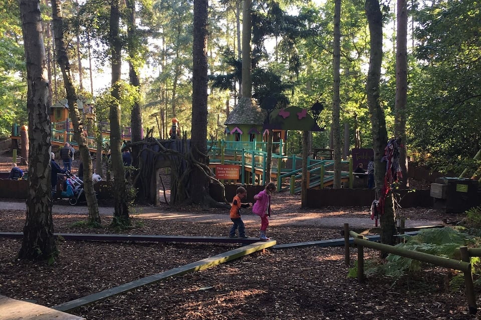 Um parque arborizado com parquinhos, mesas para piquenique e uma pequena cabana.