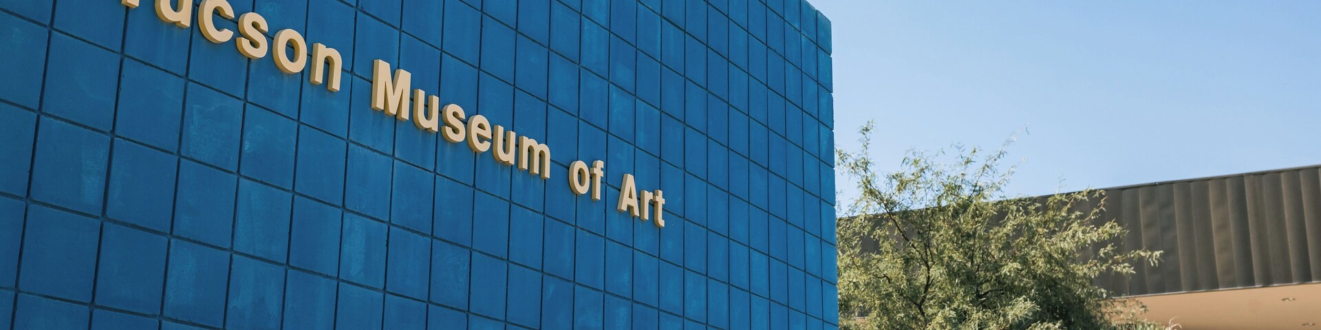 Exterior do Museu de Arte de Tucson com fachada em azulejos azuis e céu claro.