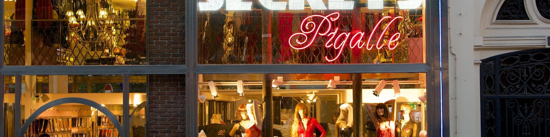 Vitrine com manequins exibindo roupas e um letreiro de neon com a inscrição "SECRETS Pygalle".