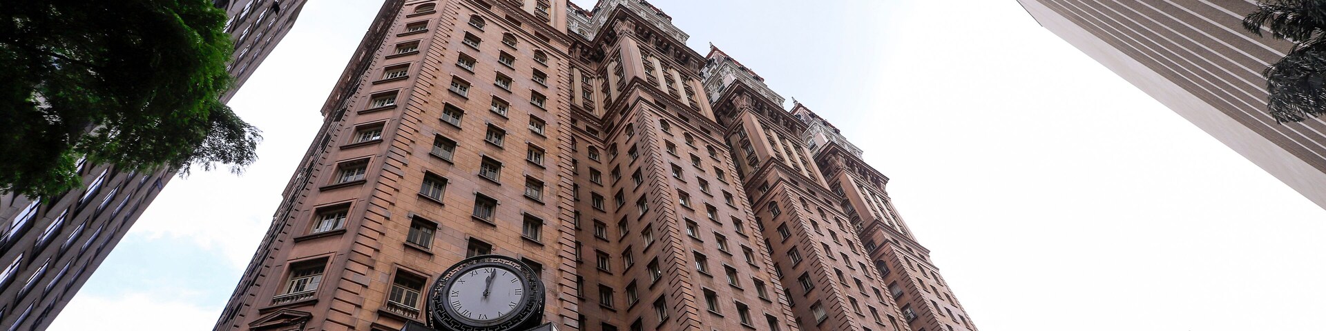 Um edifício alto e histórico com um relógio em um mastro à frente.