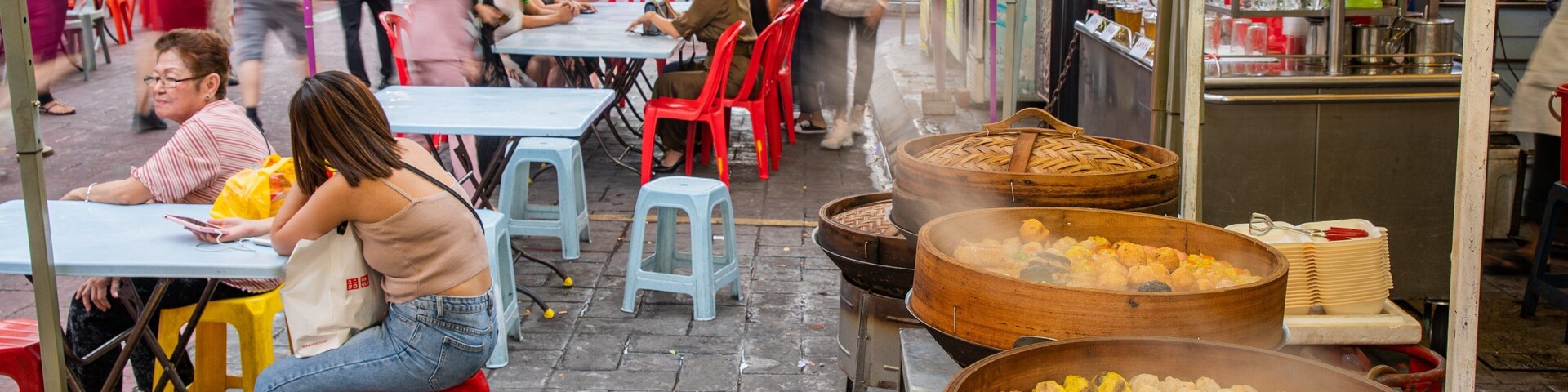 Um mercado de rua movimentado, com pessoas refeijando em mesas, barracas de comida e grandes panelas de cozinha.