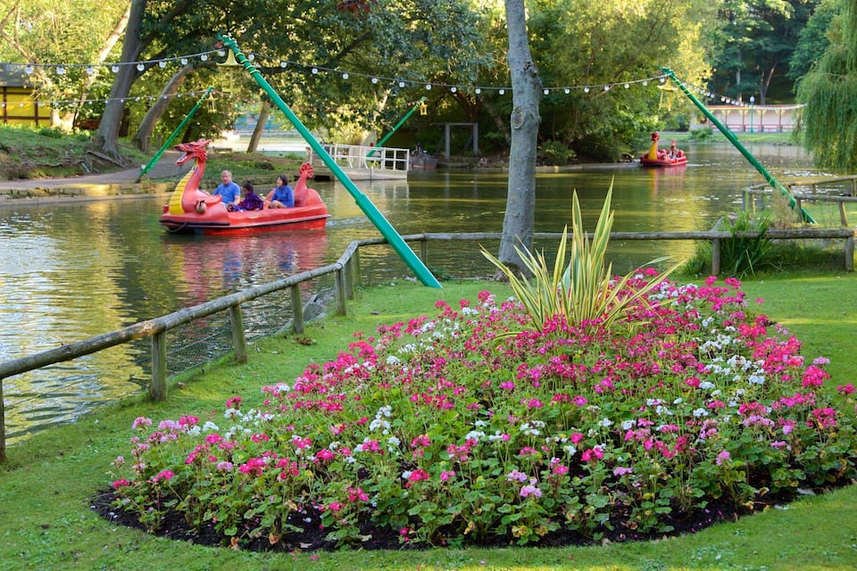 Um rio com barcos, uma ponte de madeira e um canteiro de flores.