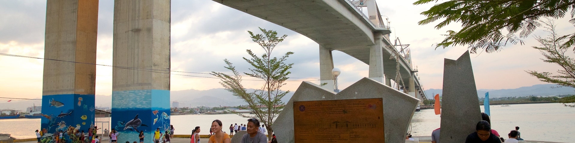 Uma ponte com uma placa, pessoas sentadas em degraus e um rio.