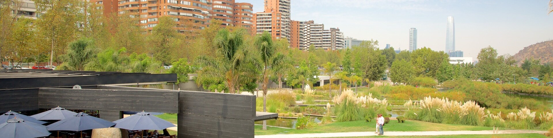 Um parque com área de refeições ao ar livre, um lago e edifícios altos ao fundo.