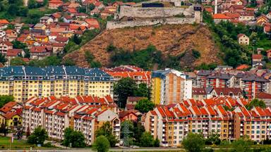 Uma cidade com edifícios coloridos, uma colina notável com uma fortaleza e um rio ao primeiro plano.