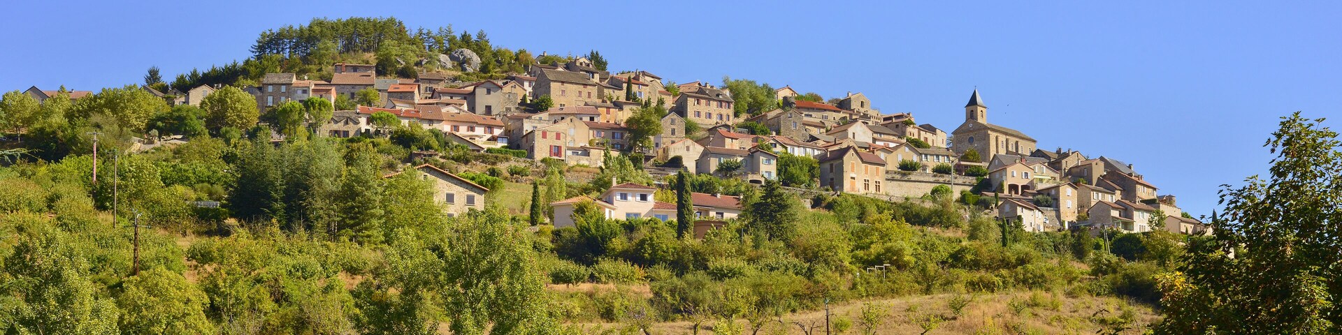Uma aldeia numa encosta, com casas de pedra tradicionais, uma igreja e vegetação exuberante.
