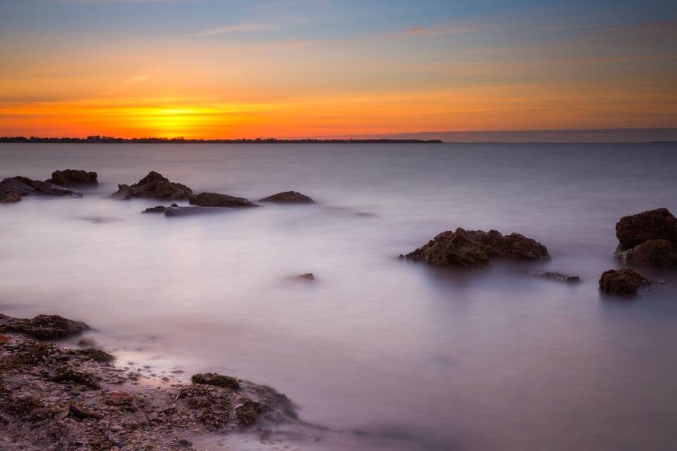 Pôr do sol sobre uma costa rochosa com águas calmas.