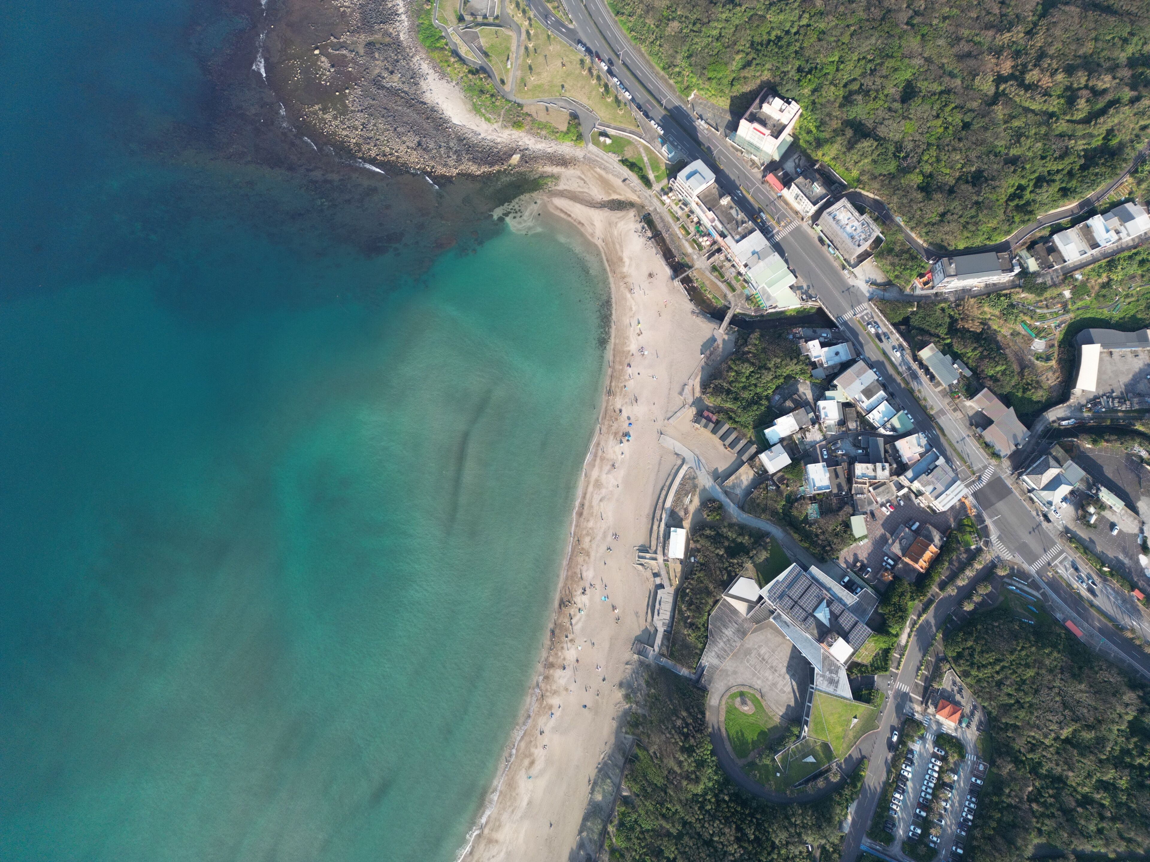 Vista aérea de uma cidade costeira com praia, águas turquesa cristalinas e uma mistura de edifícios residenciais e comerciais.