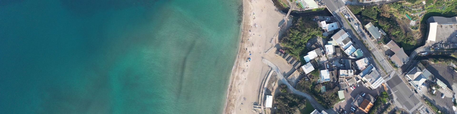 Vista aérea de uma cidade costeira com praia, águas turquesa cristalinas e uma mistura de edifícios residenciais e comerciais.