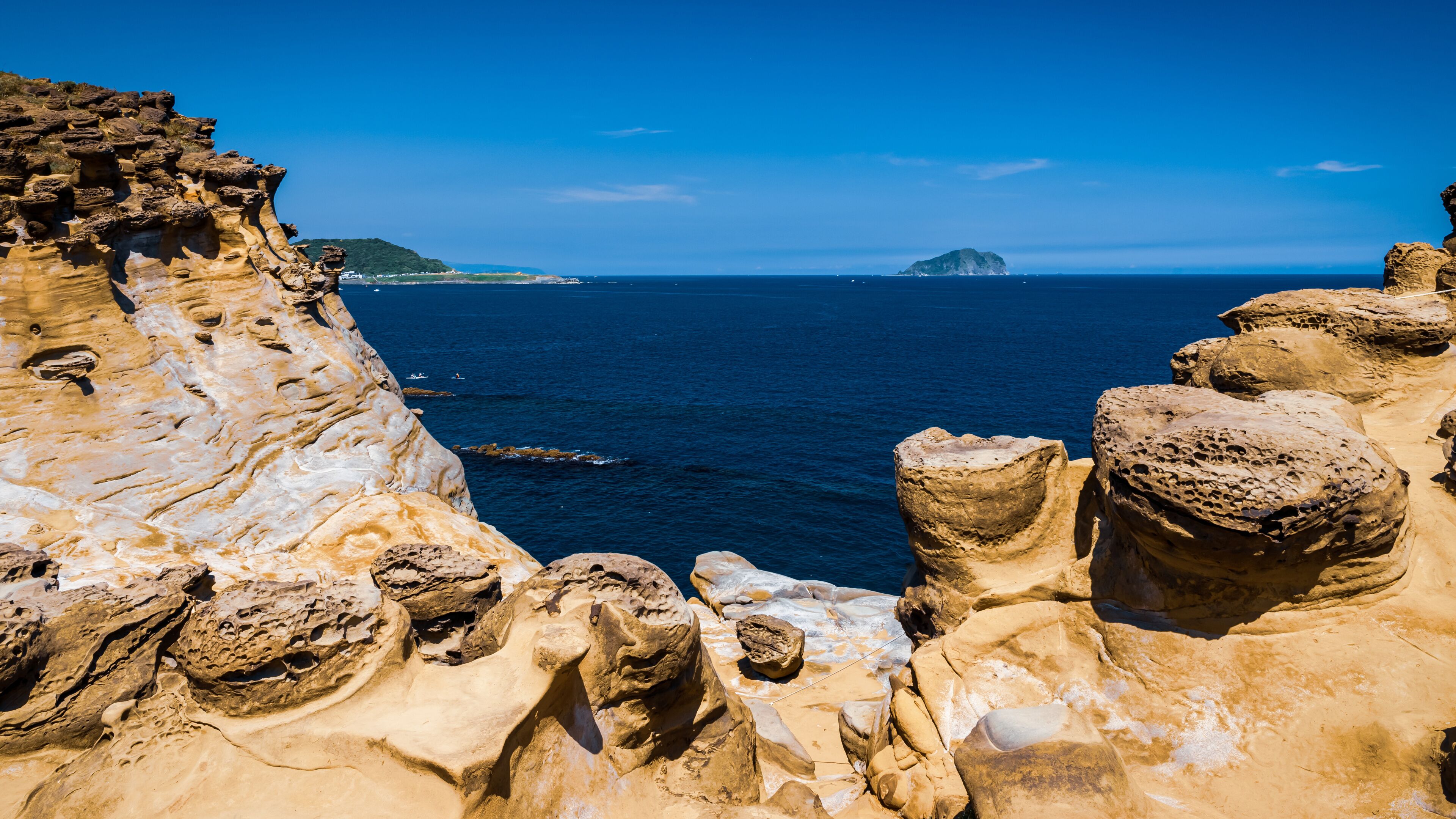 Paisagem costeira com falésias rochosas, mar azul cristalino e uma ilha ao longe.