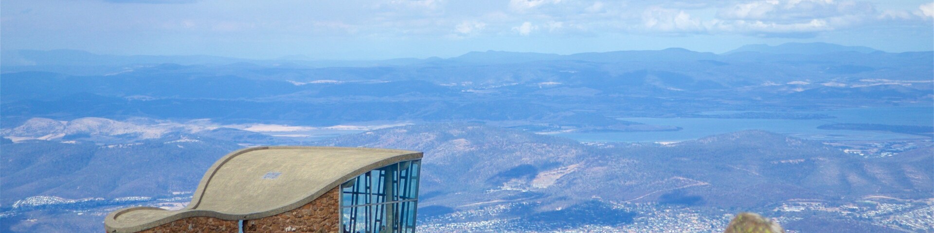 Um edifício de pedra com telhado curvo, com vista para um vale e um lago.
