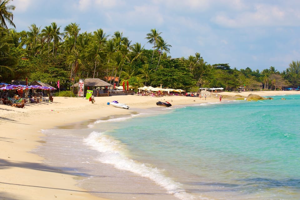 Uma praia tropical com águas turquesa cristalinas, palmeiras e guarda-sóis.