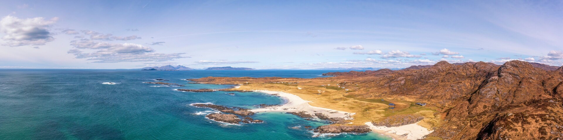 Paisagem costeira com uma praia arenosa, falésias rochosas e um mar azul cristalino.