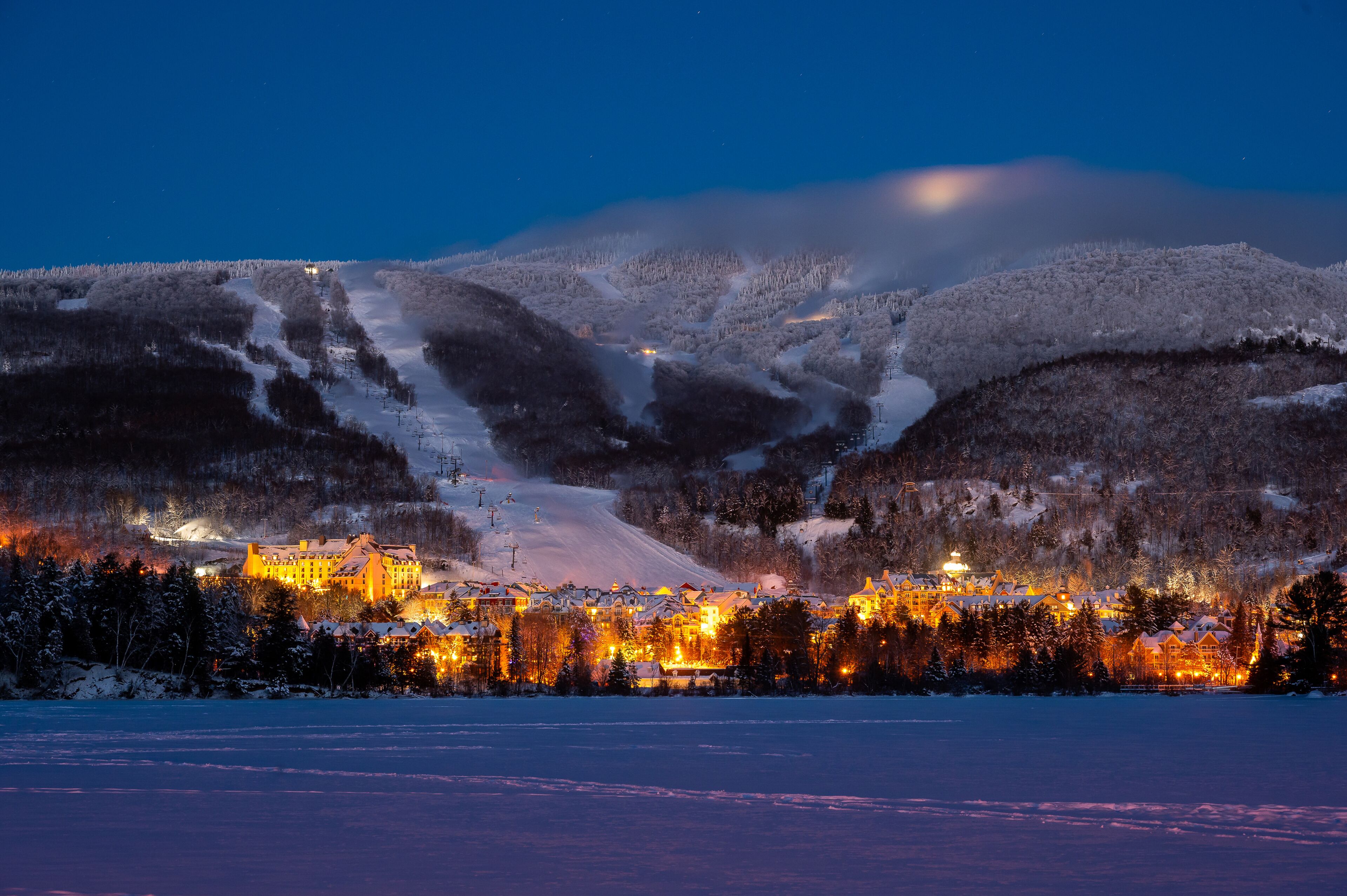 Cordilheira nevada ao entardecer, com uma cidade iluminada em primeiro plano.