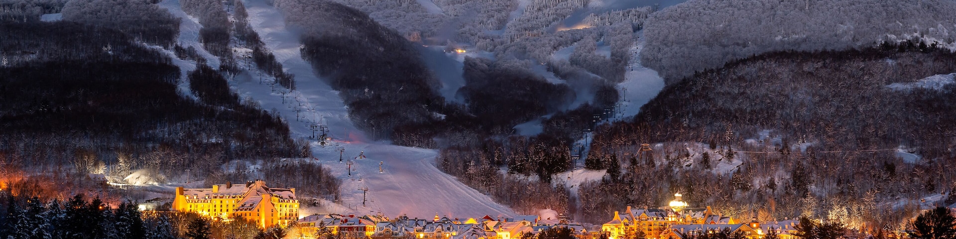 Cordilheira nevada ao entardecer, com uma cidade iluminada em primeiro plano.