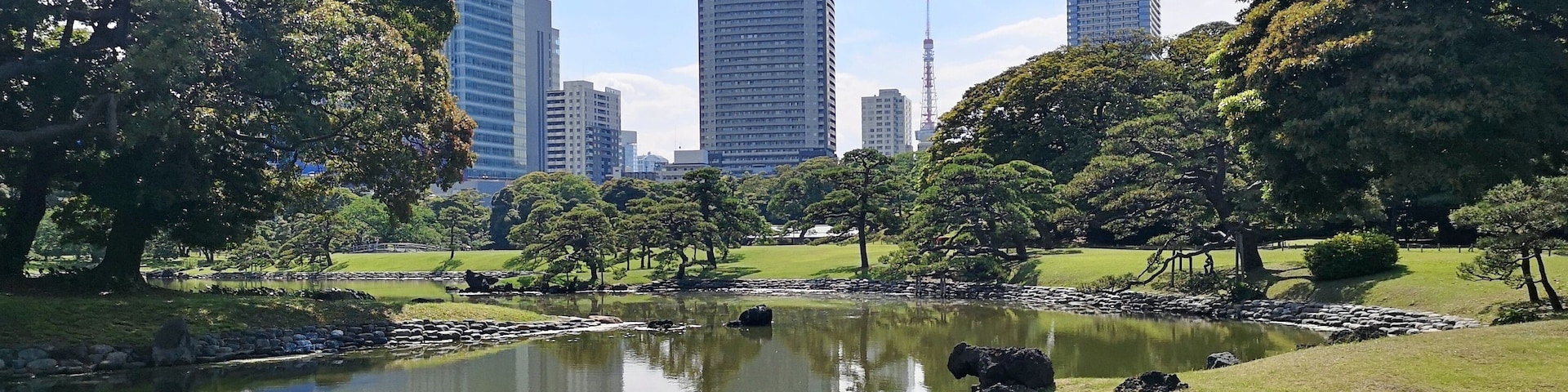 Um parque com lago, árvores e o horizonte da cidade ao fundo.