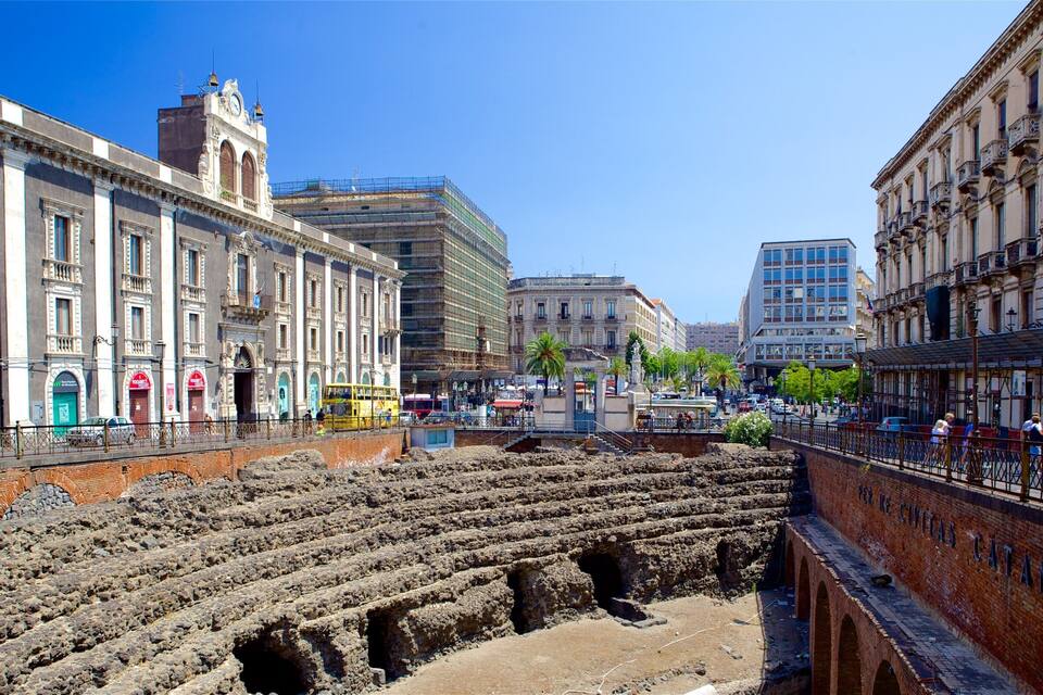 Um sítio arqueológico com ruínas antigas e edifícios modernos ao fundo.