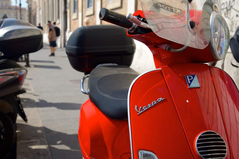 Uma scooter Vespa vermelha estacionada numa rua da cidade.