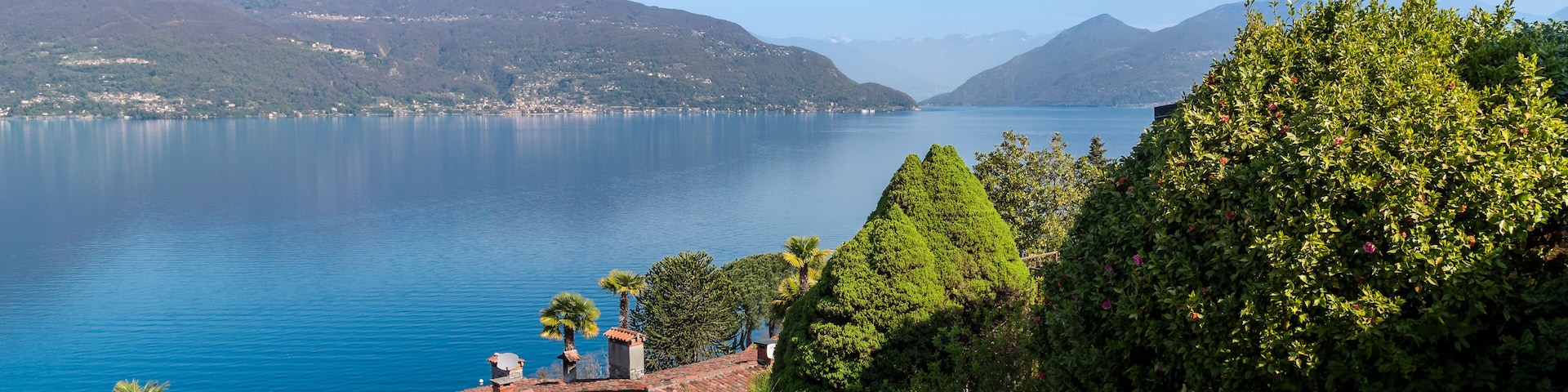 Um lago cercado por montanhas, com um edifício de telhado vermelho e vegetação exuberante em primeiro plano.