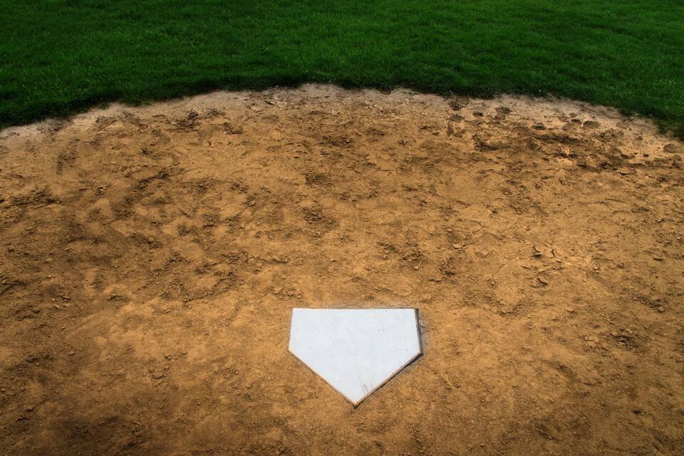 Um campo de beisebol com área interna branca e área externa verde.