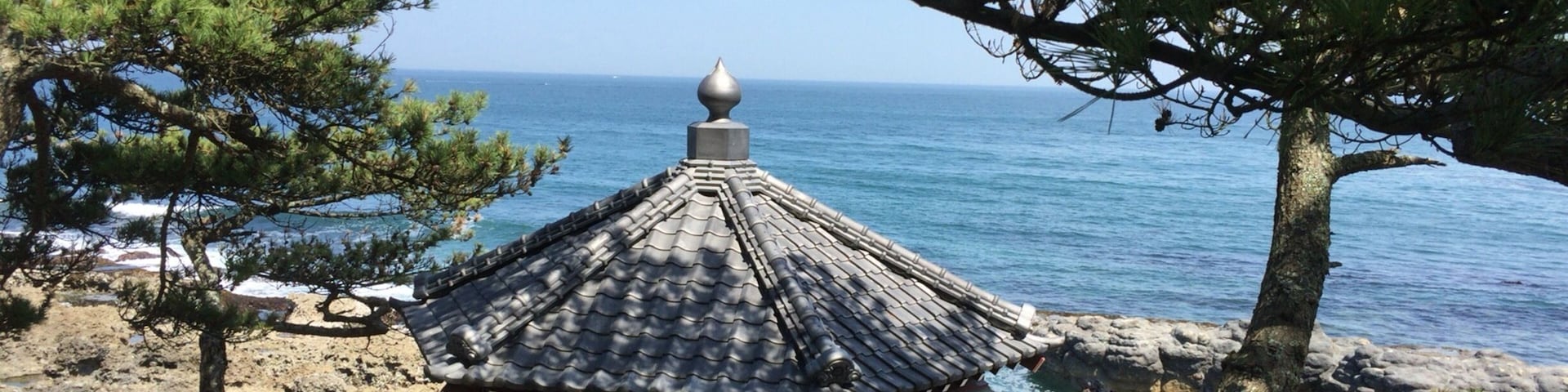 Um pavilhão japonês tradicional com telhado de telhas e vista para o mar.