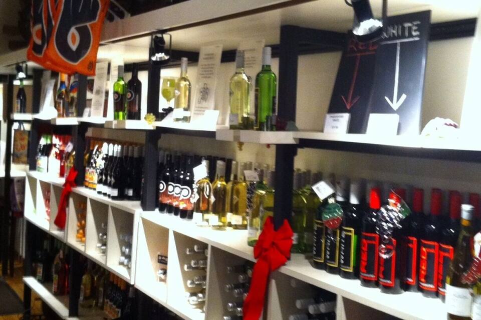 Estantes repletas de diversas garrafas de bebidas alcoólicas, incluindo vinho e destilados, algumas adornadas com laços vermelhos.