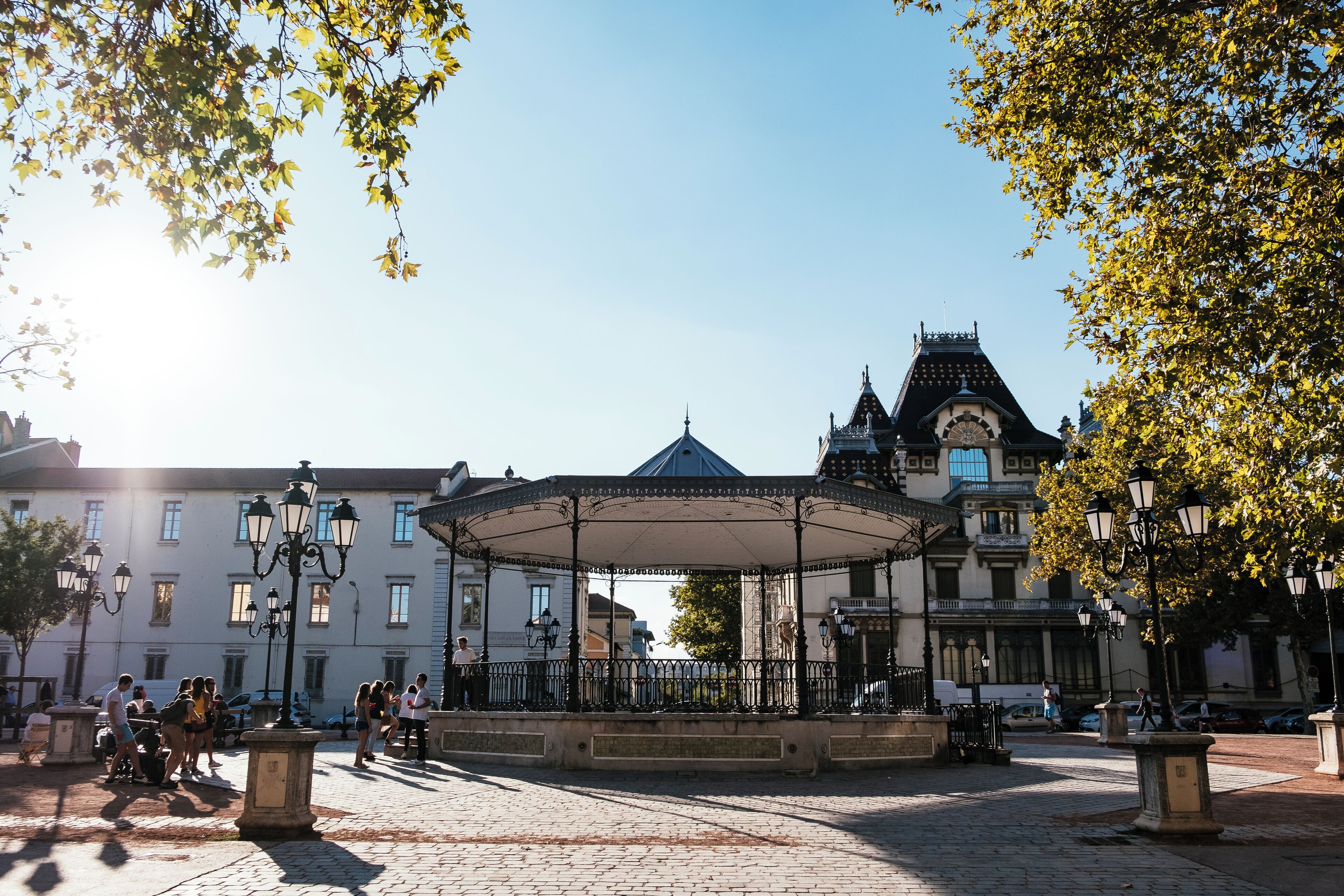Uma praça de paralelepípedos com um coreto, edifícios históricos e árvores.